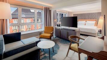 Quarto de hotel com sofá, poltrona, mesa de jantar, televisão e cama com cabeceira.