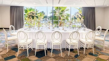 Uma sala de conferência com uma grande mesa redonda, cadeiras brancas e centros de mesa florais.