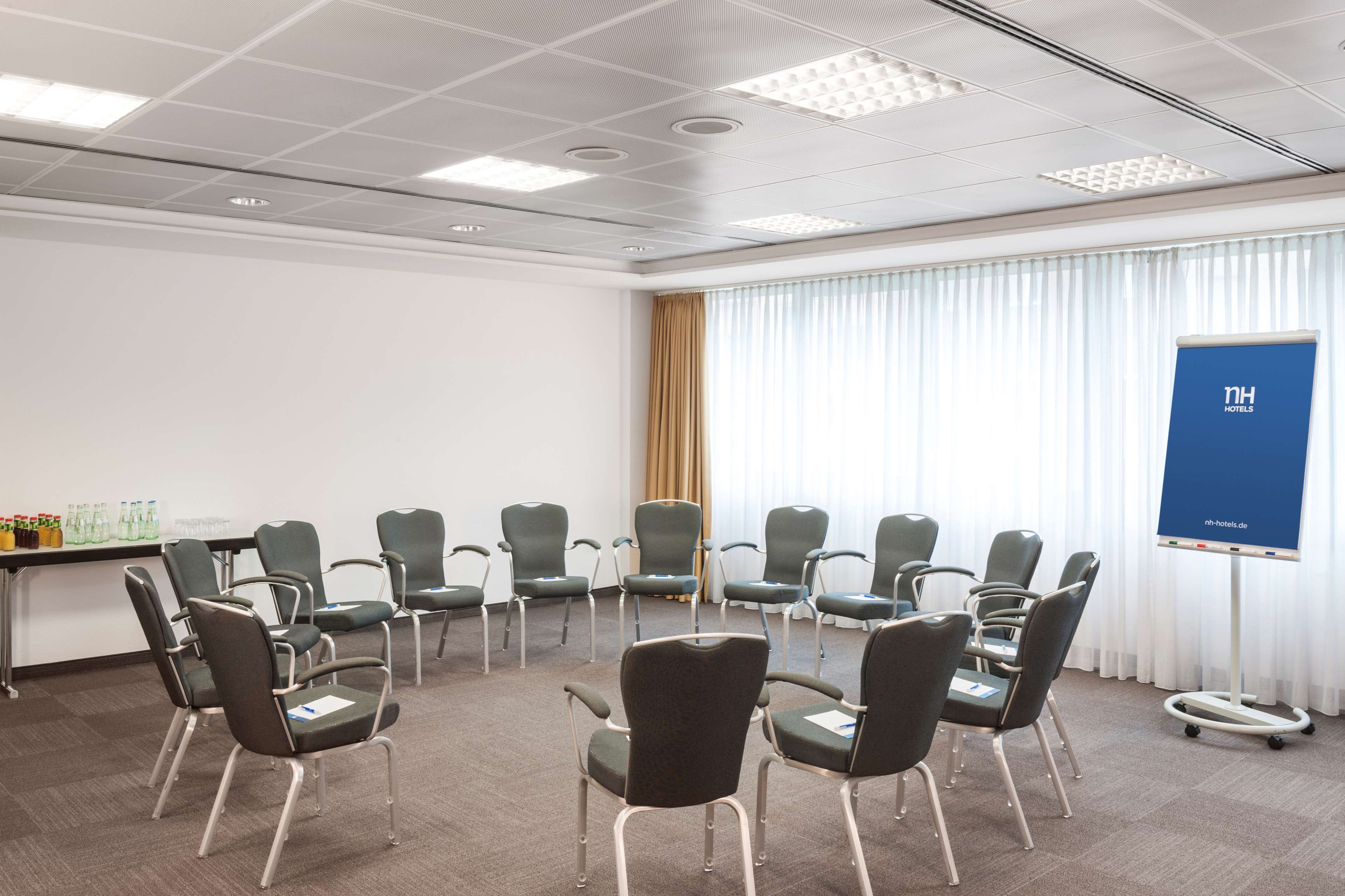 Uma sala de conferência com uma mesa redonda, cadeiras, quadro branco e tela de projeção.