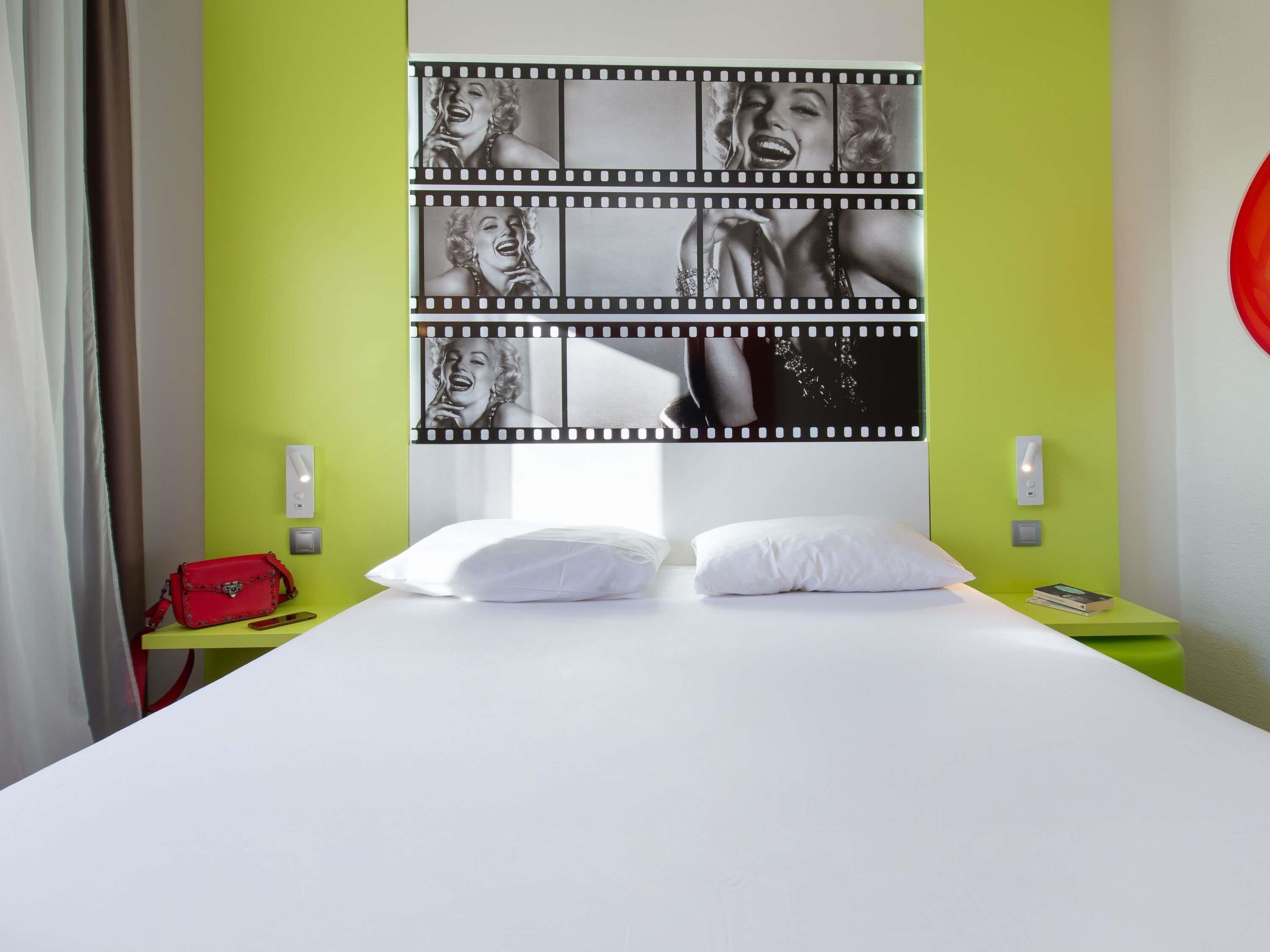 Cama com lençóis brancos, bolsa vermelha e uma obra de arte com tema de filme na parede.