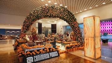 Um saguão de hotel com um arco floral grande, plantas em vasos e uma mesa central decorativa.