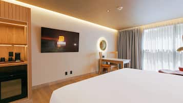 Quarto de hotel com cama, televisão na parede, escrivaninha com cadeira e janela com cortinas.