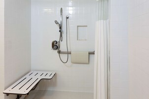 Área de duche com chuveiro manual, toalheiro fixado na parede e um banco.