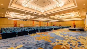 Uma sala de conferências ampla com fileiras de cadeiras azuis, um palco e um tapete com padrão azul e amarelo.