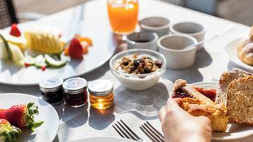 Uma mesa de café da manhã com pratos de comida, incluindo morangos, uma tigela de cereais e um copo de suco de laranja.