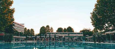 Piscina com reflexo límpido, rodeada por árvores e edifícios.