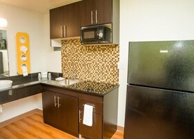 Uma cozinha compacta com armários de madeira escura, micro-ondas, geladeira e painel de azulejos.
