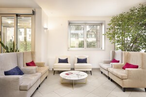 Uma sala de estar moderna com dois sofás, duas poltronas, uma mesa de centro redonda e uma grande janela com vista para o verde.