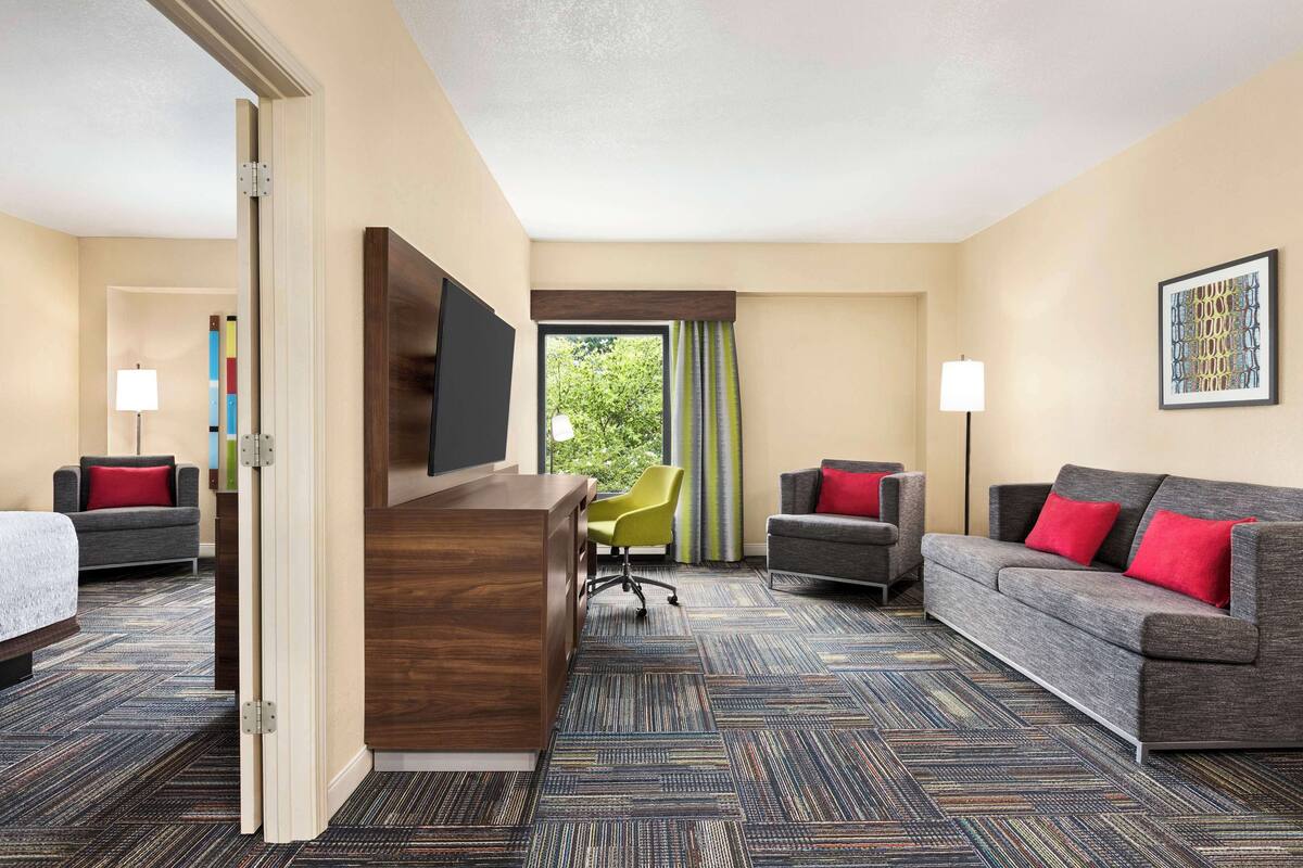 Quarto de hotel com uma secretária, dois sofás, uma poltrona e uma televisão.