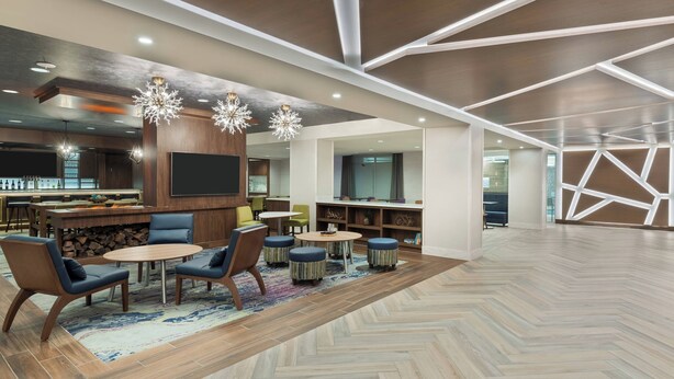 Um lobby de hotel moderno com área de bar, assentos e uma grande tela de televisão.