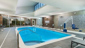 Piscina interior moderna com água azul cristalina, rodeada por espreguiçadeiras e uma área envidraçada.