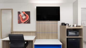 Quarto de hotel com escrivaninha, cadeira, televisão de tela plana, obras de arte, micro-ondas e uma pequena geladeira.