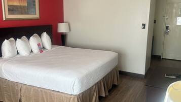 Quarto de hotel com uma cama grande, uma poltrona verde, um abajur e um quadro na parede.