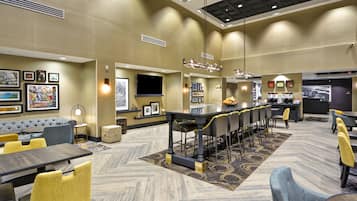 Um hall de hotel moderno com um bar, áreas de estar e obras de arte nas paredes.