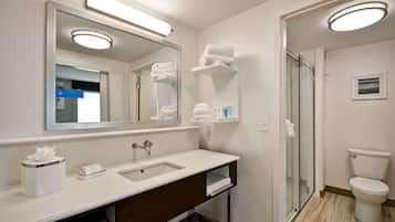Uma casa de banho moderna com lavatório branco, toucador escuro, cabine de duche em vidro e sanita.