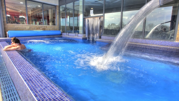 Piscina interior com escorrega, água azul cristalina e borda revestida em azulejos.
