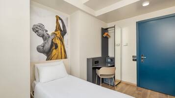 Quarto de hotel com cama, escrivaninha, cadeira, guarda-roupa e uma obra de arte pendurada na parede.