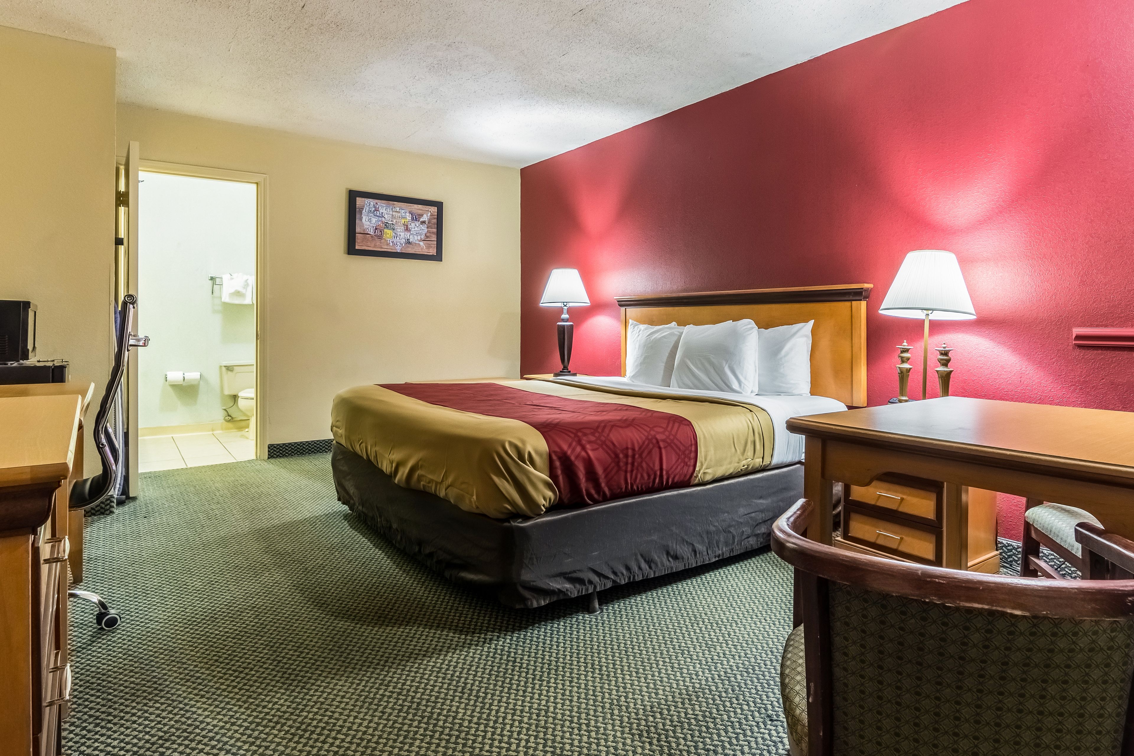 Quarto de hotel com cama, duas luminárias de cabeceira, uma escrivaninha e uma cadeira.