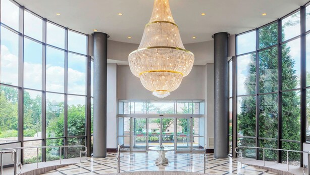 Um hall amplo com grandes janelas, um lustre central e piso de azulejos.