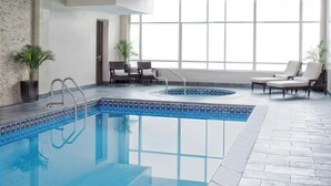 Piscina interior com água azul cristalina, rodeada por espreguiçadeiras e plantas em vasos.