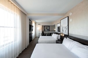 Quarto de hotel com duas camas, uma escrivaninha e uma cadeira.
