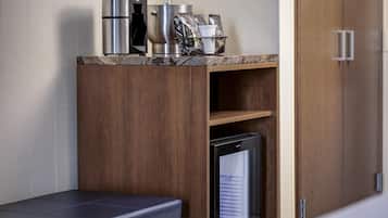 Uma cozinha compacta com cafeteira, chaleira e cápsulas de café no balcão.