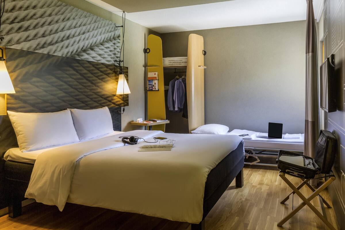 Quarto de hotel com cama, mesa de cabeceira, abajur e escrivaninha com cadeira.