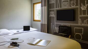 Quarto de hotel com uma cama, um laptop, um par de óculos, um livro e uma televisão na parede.