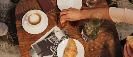 Uma mesa de madeira com um croissant, uma xícara de café, um copo de água, uma garrafa de água e uma revista.