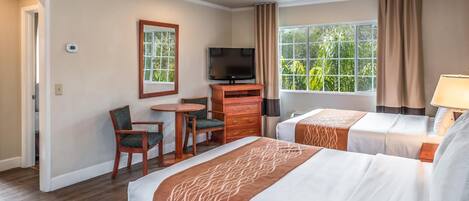 Quarto de hotel com duas camas, televisão, escrivaninha com cadeira e janela com cortinas.