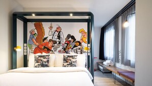Quarto de hotel com uma cama grande, uma mesinha de cabeceira, um banco e um mural retratando um grupo de pessoas.