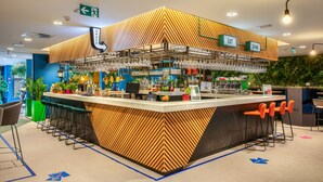 Uma área de bar moderna com design em padrão geométrico de cunhas, banquetas e uma variedade de garrafas e copos.