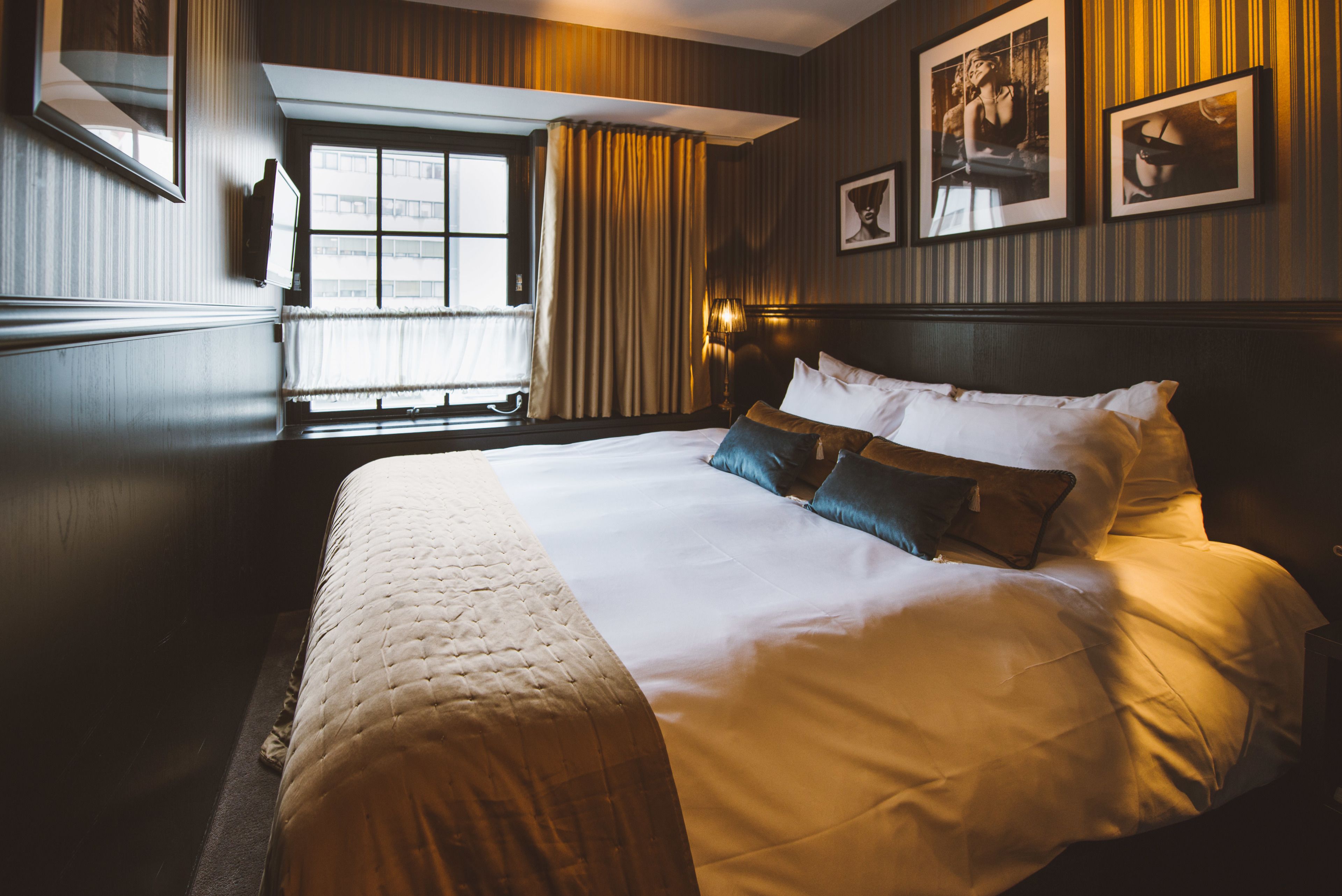Quarto de hotel com uma cama grande, uma janela com cortinas e quadros na parede.