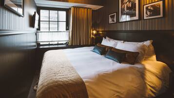 Quarto de hotel com uma cama grande, uma janela com cortinas e quadros na parede.