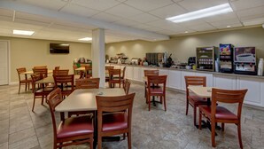 Uma sala de jantar com mesas e cadeiras de madeira, um balcão com uma máquina de café e uma televisão fixada na parede.
