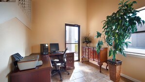 Escritório em casa com mesa, computador, impressora e uma grande planta em vaso.