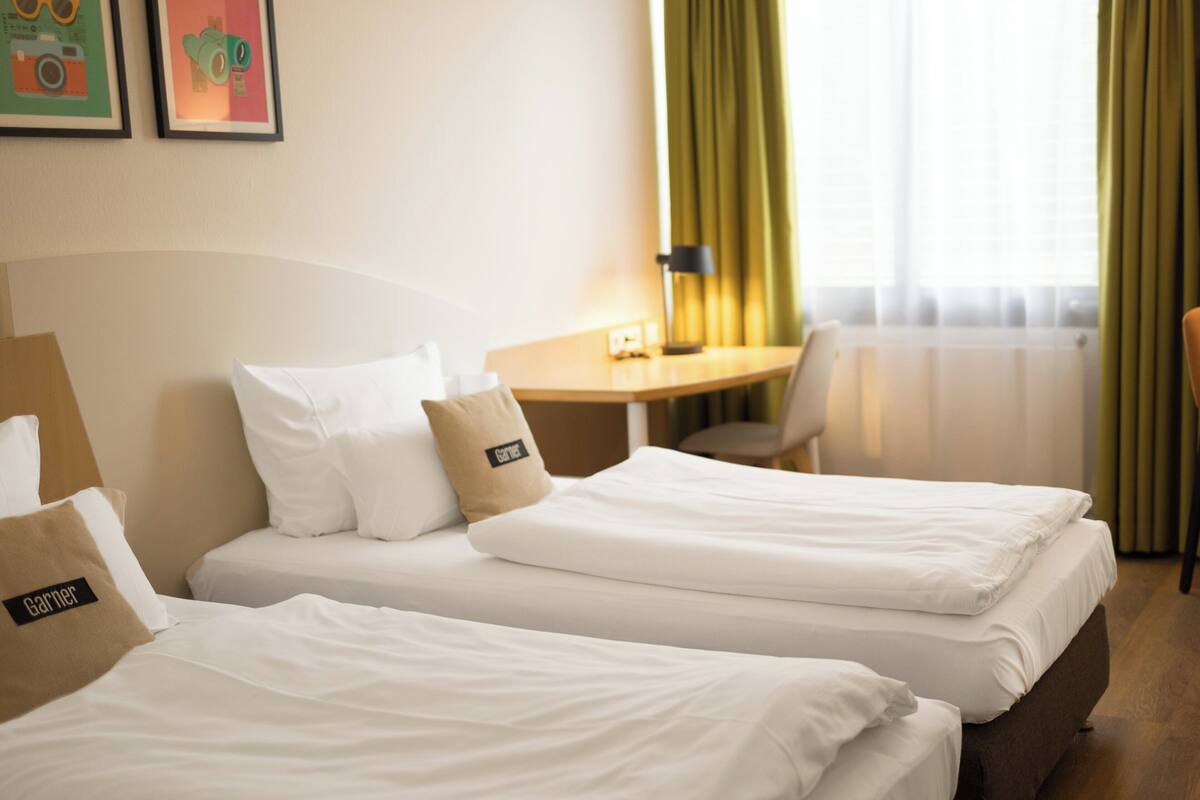 Quarto de hotel com duas camas, uma mesa e uma cadeira.