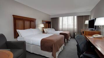 Quarto de hotel com duas camas, uma mesa de trabalho com telefone, uma cadeira e uma televisão.