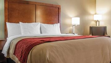 Quarto de hotel com uma cama grande, cabeceira de madeira, duas luminárias de cabeceira e um cobertor vermelho.