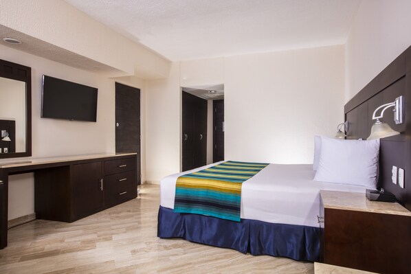 Quarto de hotel com cama, escrivaninha, televisão de tela plana e guarda-roupa.