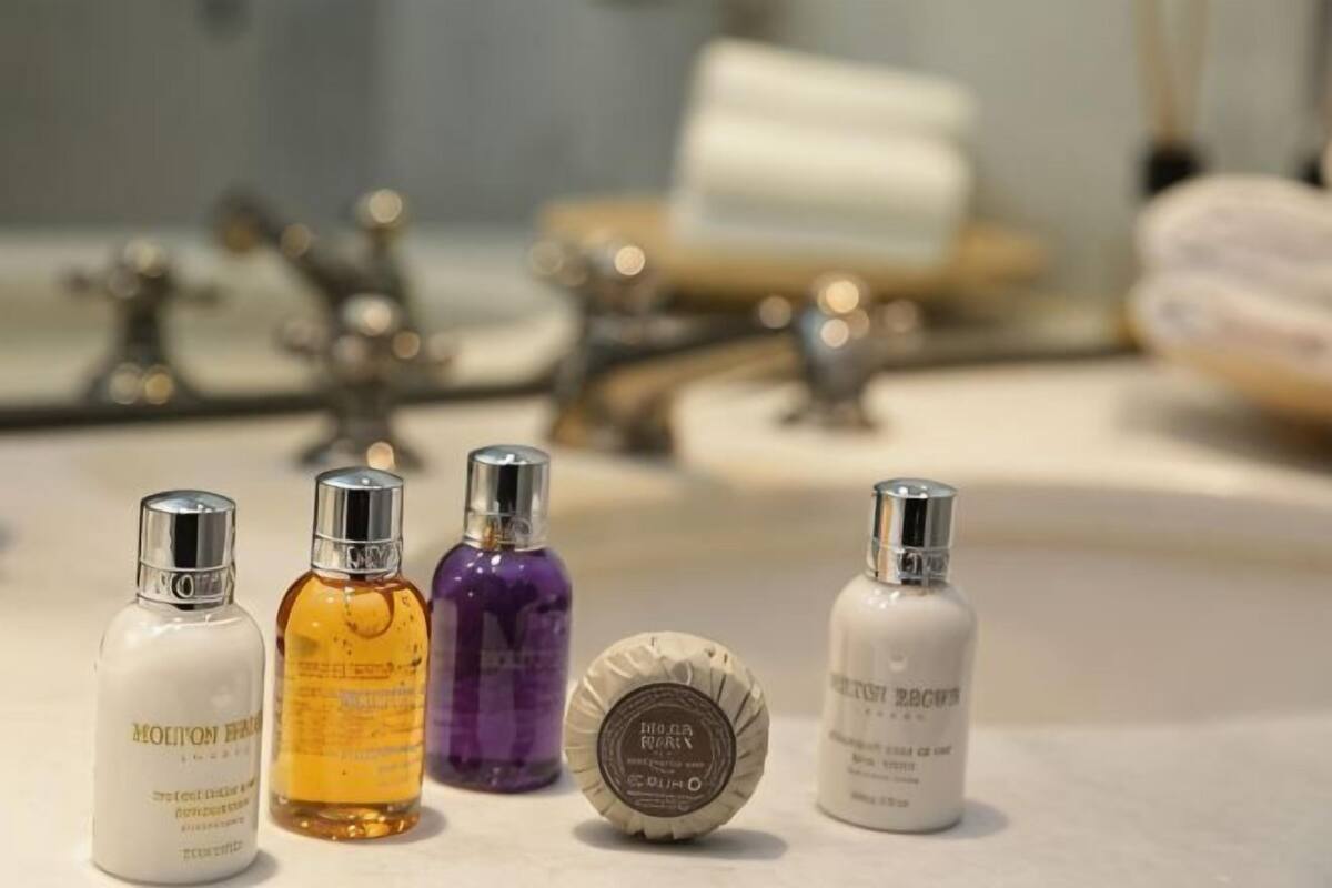Um banheiro com espelho, pia e quatro frascos de produtos de higiene pessoal.
