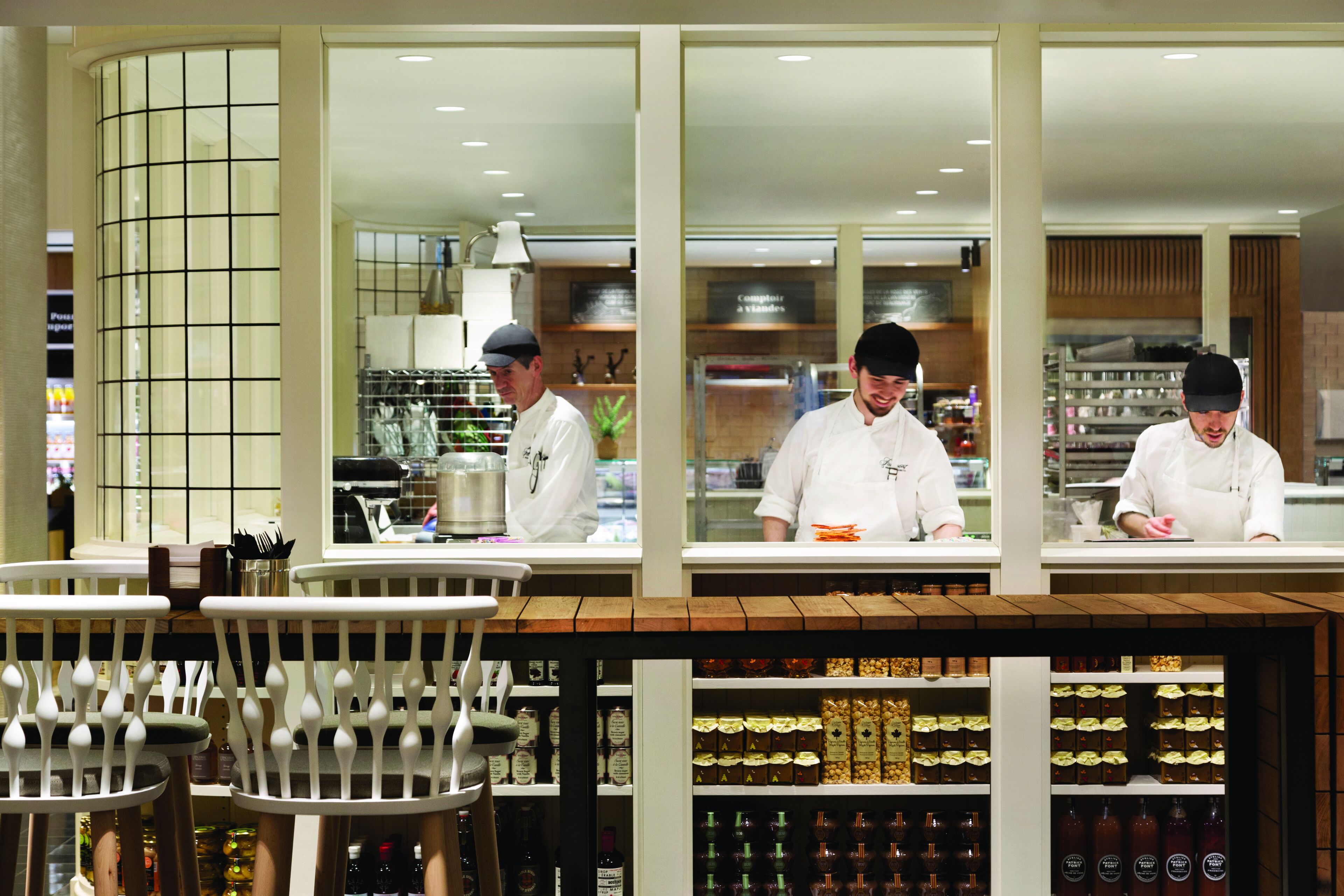 Interior de restaurante com área de bar, prateleiras com garrafas e três garçons.