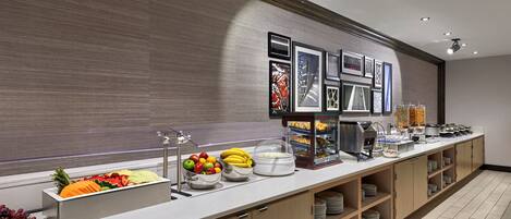 Uma área de buffet com diversos alimentos, incluindo frutas, vegetais e pratos prontos.