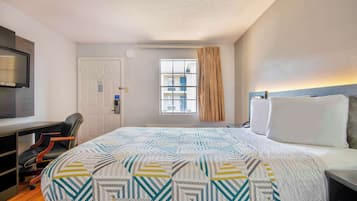 Quarto de hotel com cama, escrivaninha, cadeira, televisão, janela com cortinas e vista para edifícios.