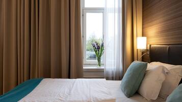 Quarto de hotel com uma cama grande, cortinas bege, uma janela com vista e um abajur.