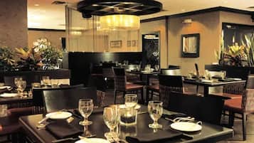Um restaurante com mesas postas para refeições, com decoração moderna, um candelabro e plantas em vasos.