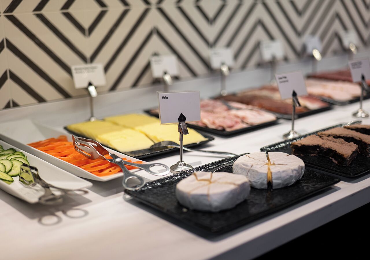 Buffet com diversos alimentos, incluindo queijos, vegetais e carnes.