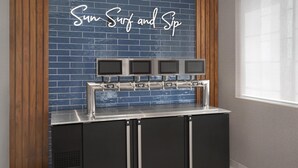 Uma área de bar com um letreiro que diz 'Sun Surf and Sip' acima de uma fileira de dispensadores de bebidas.