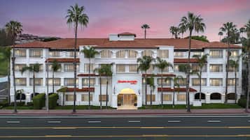 Um hotel de vários andares com telhado de telhas vermelhas, várias varandas e palmeiras.