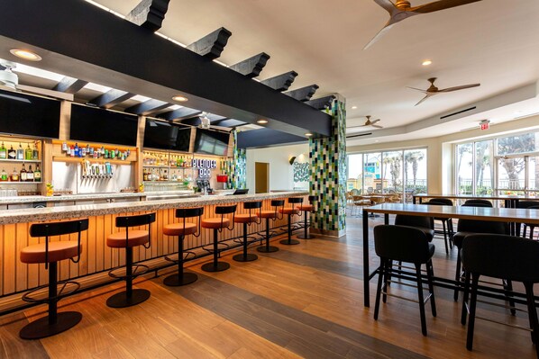 Uma área de bar moderna com um balcão comprido, vários bancos e uma variedade de garrafas e copos.